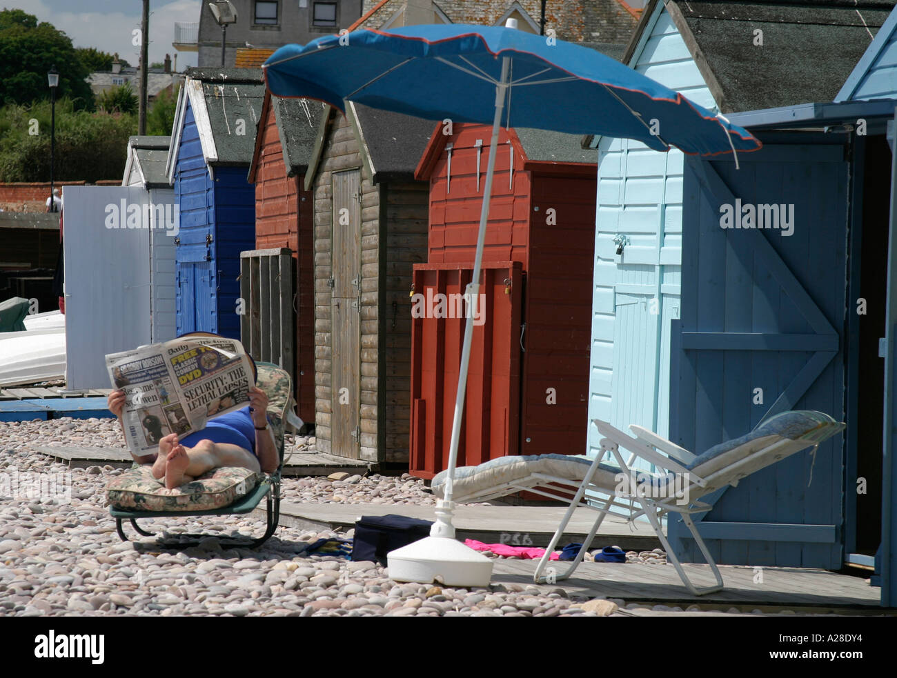 Lady reading tabloid newspaper at beach hut Budleigh Salterton Beach ...