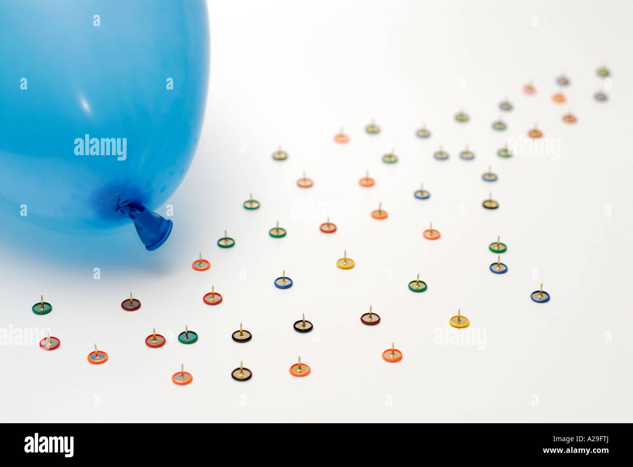 A blue balloon surrounded by coloured drawing pins on a white ...