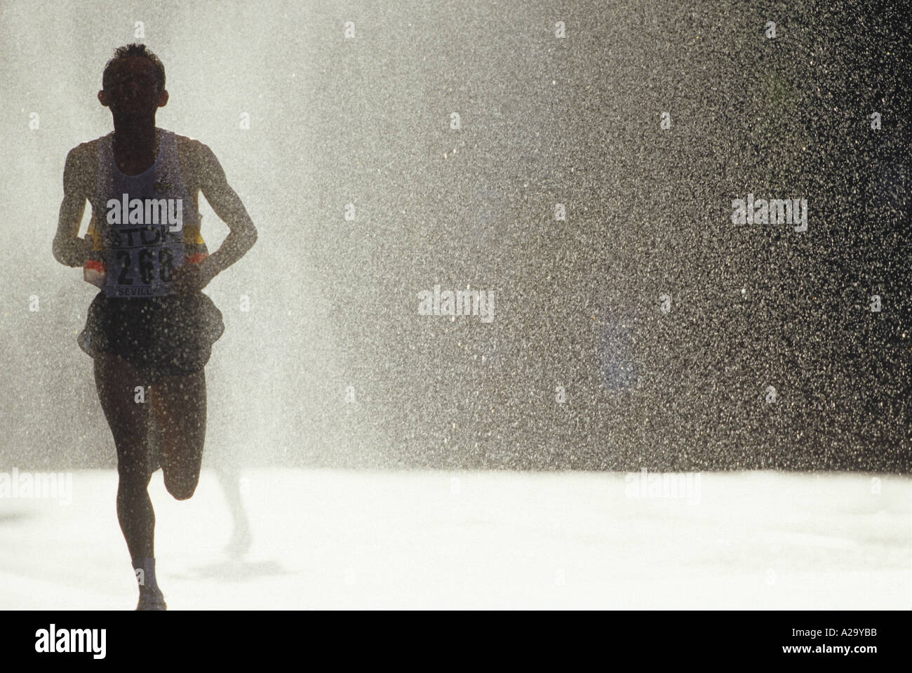 A male runner passes through a cooling water spray during a marathon ...