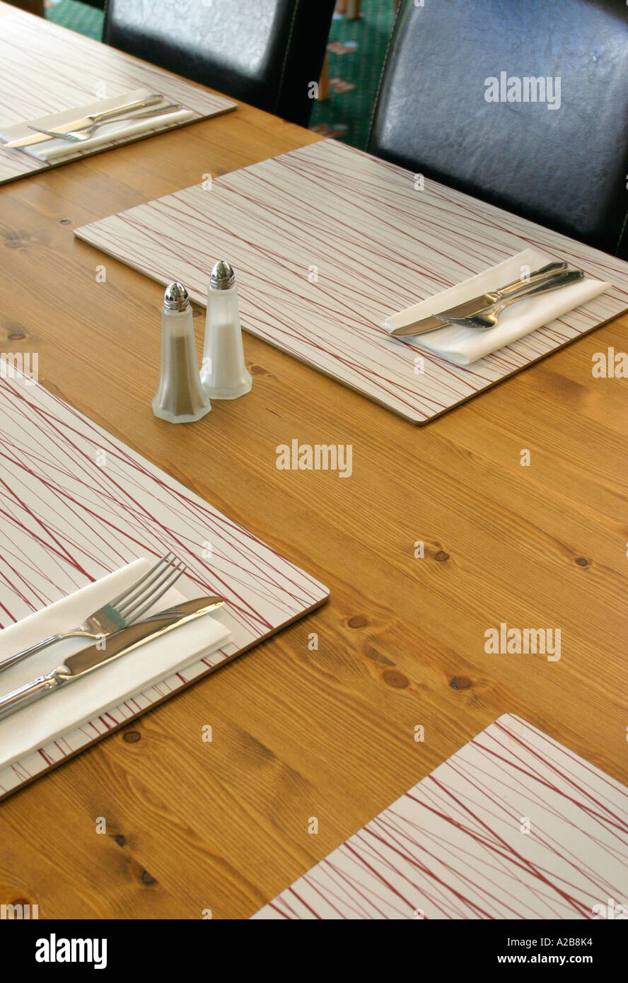 Modern wooden restaurant table showing knives, forks and condiment set ...