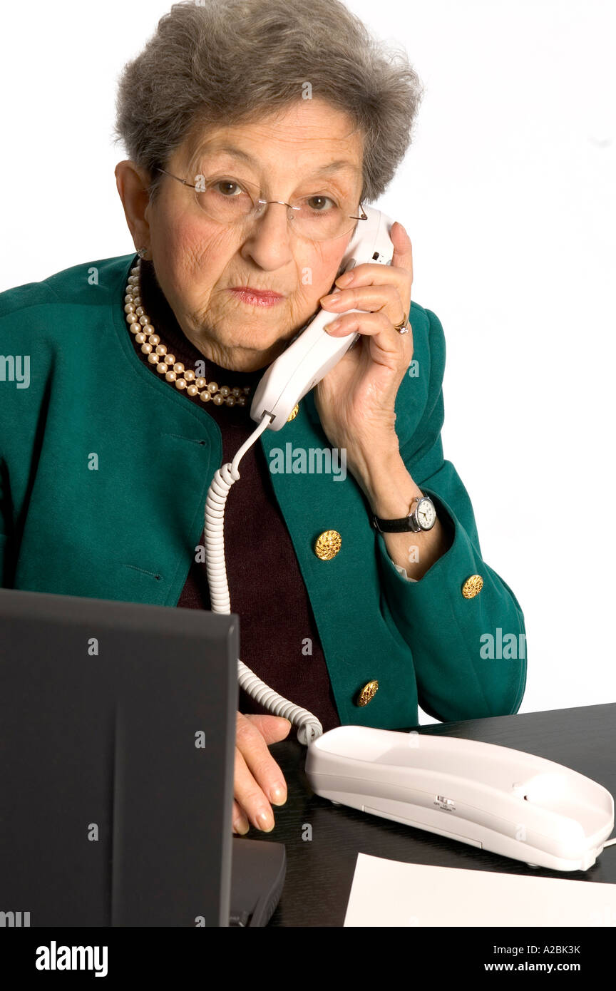 senior citizen office executive talking on phone at desk with computer ...