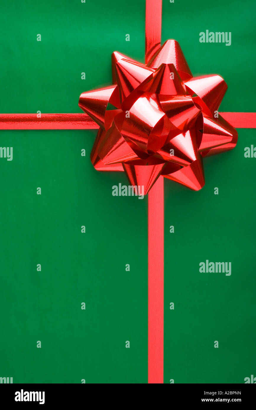 A present wrapped in green paper with red ribbons and a red foil bow ...