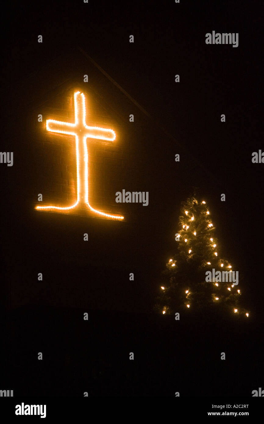 an illuminated cross on a church building near a Christmas tree Stock ...