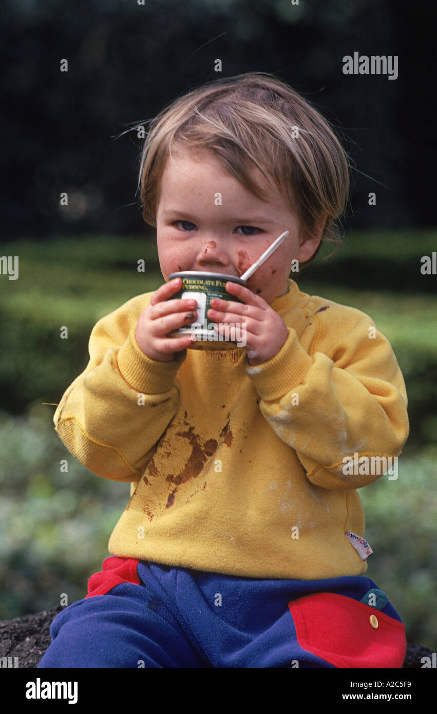 Close-up of adorable little boy sitting outside eating pudding cup and ...