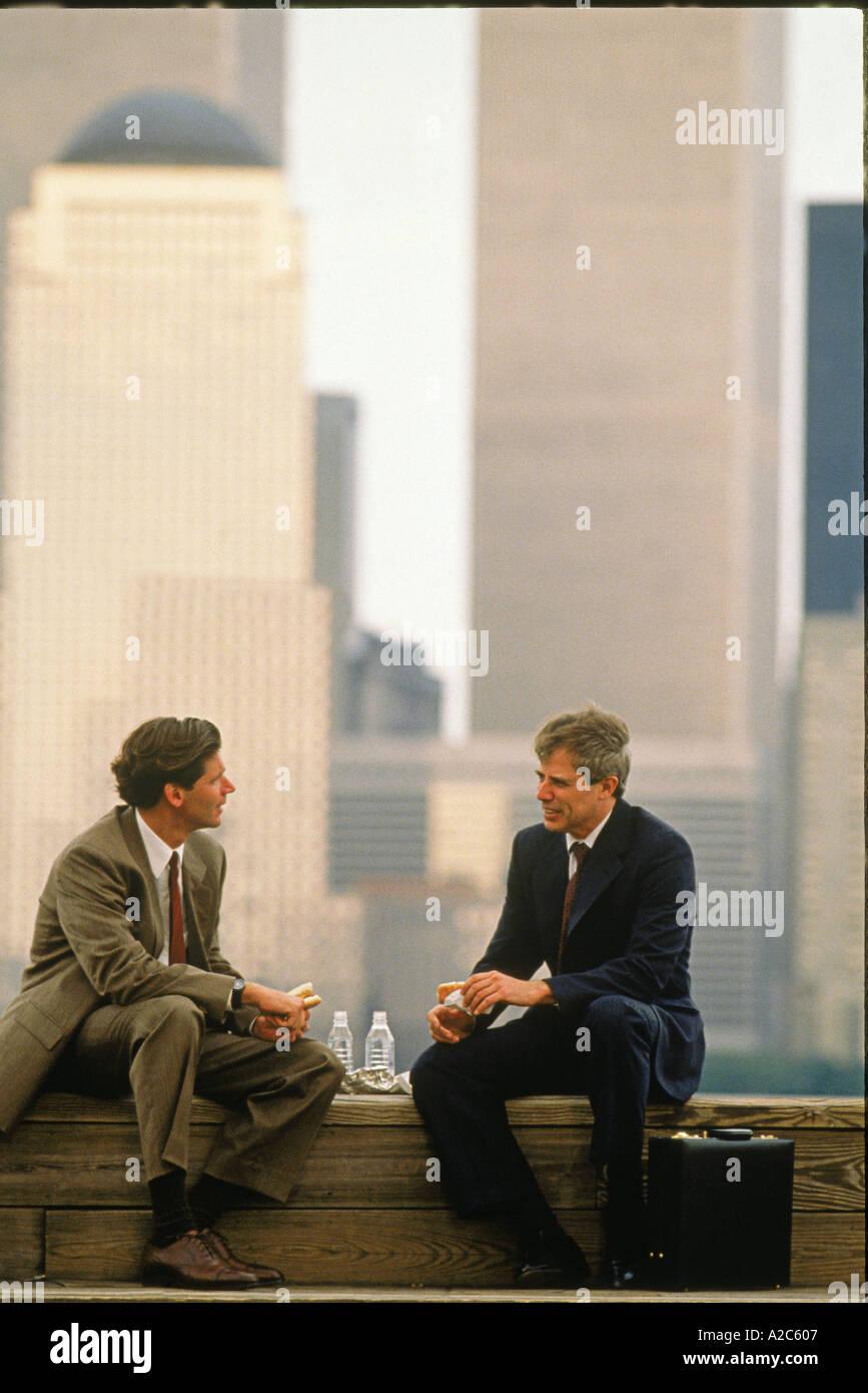Two businessmen sitting outside talking with view of city in background ...
