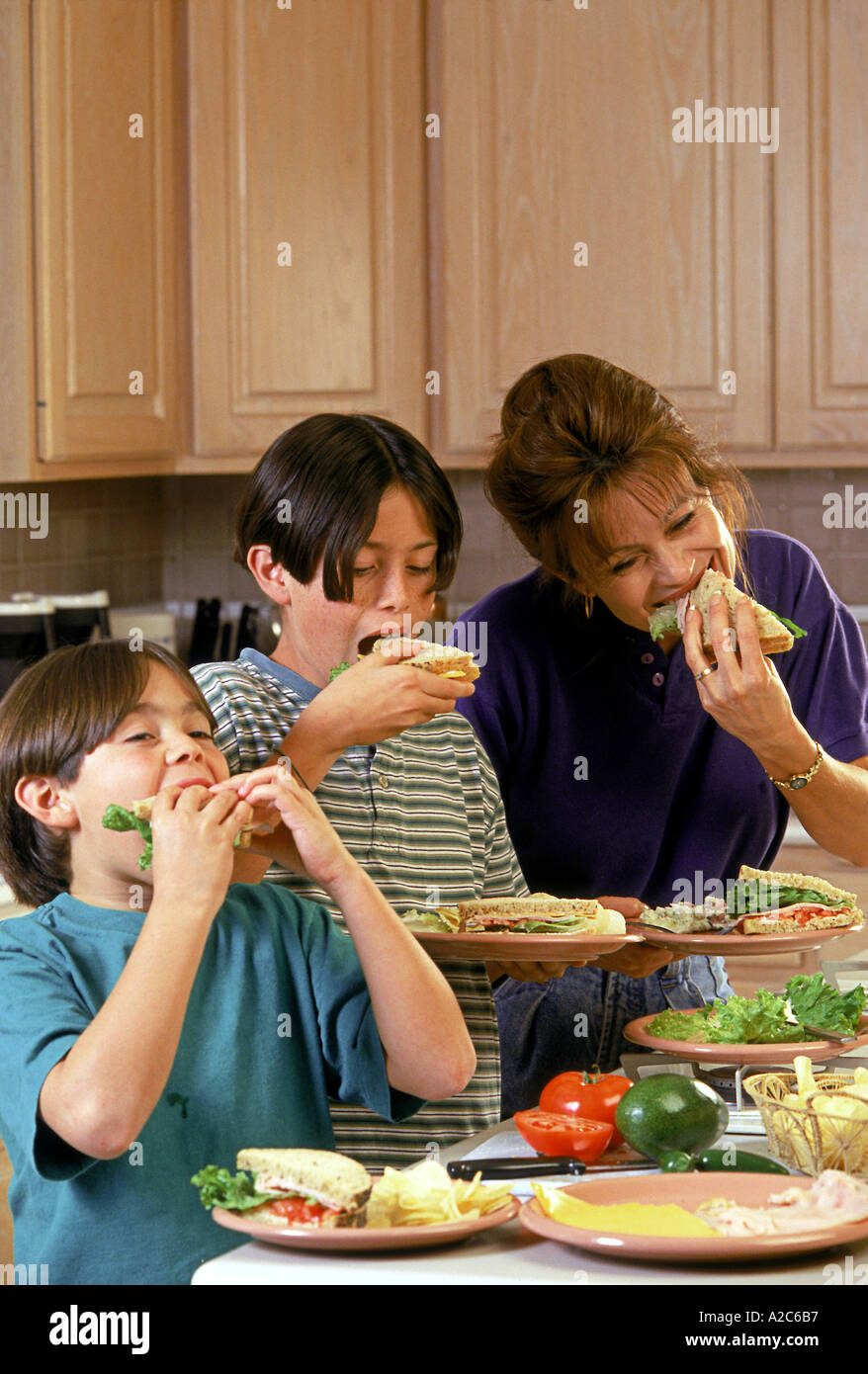 Mother and two sons eating sandwiches while standing in the kitchen ...