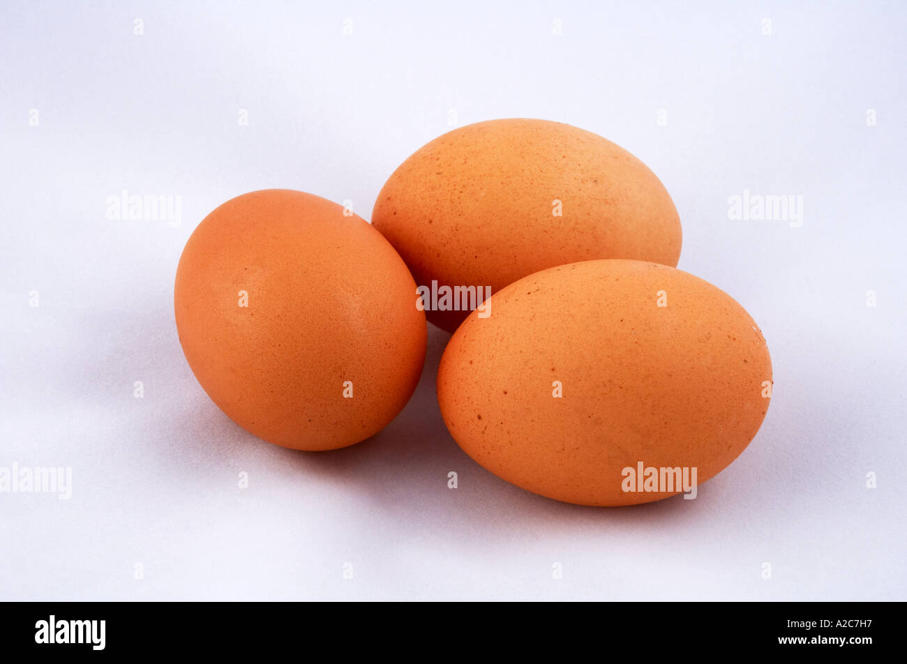 A group of three fresh whole brown hens eggs with the shell of each egg ...