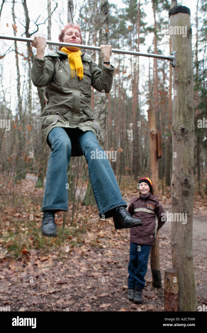 mother chinning the bar in a forest while her young son is watching ...