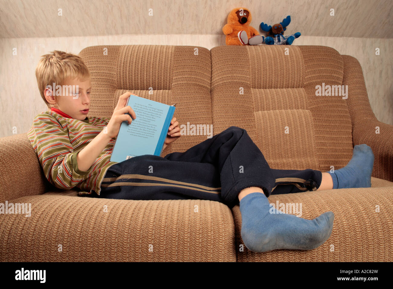 portrait of a young fair boy lying on a sofa and reading a book Stock ...