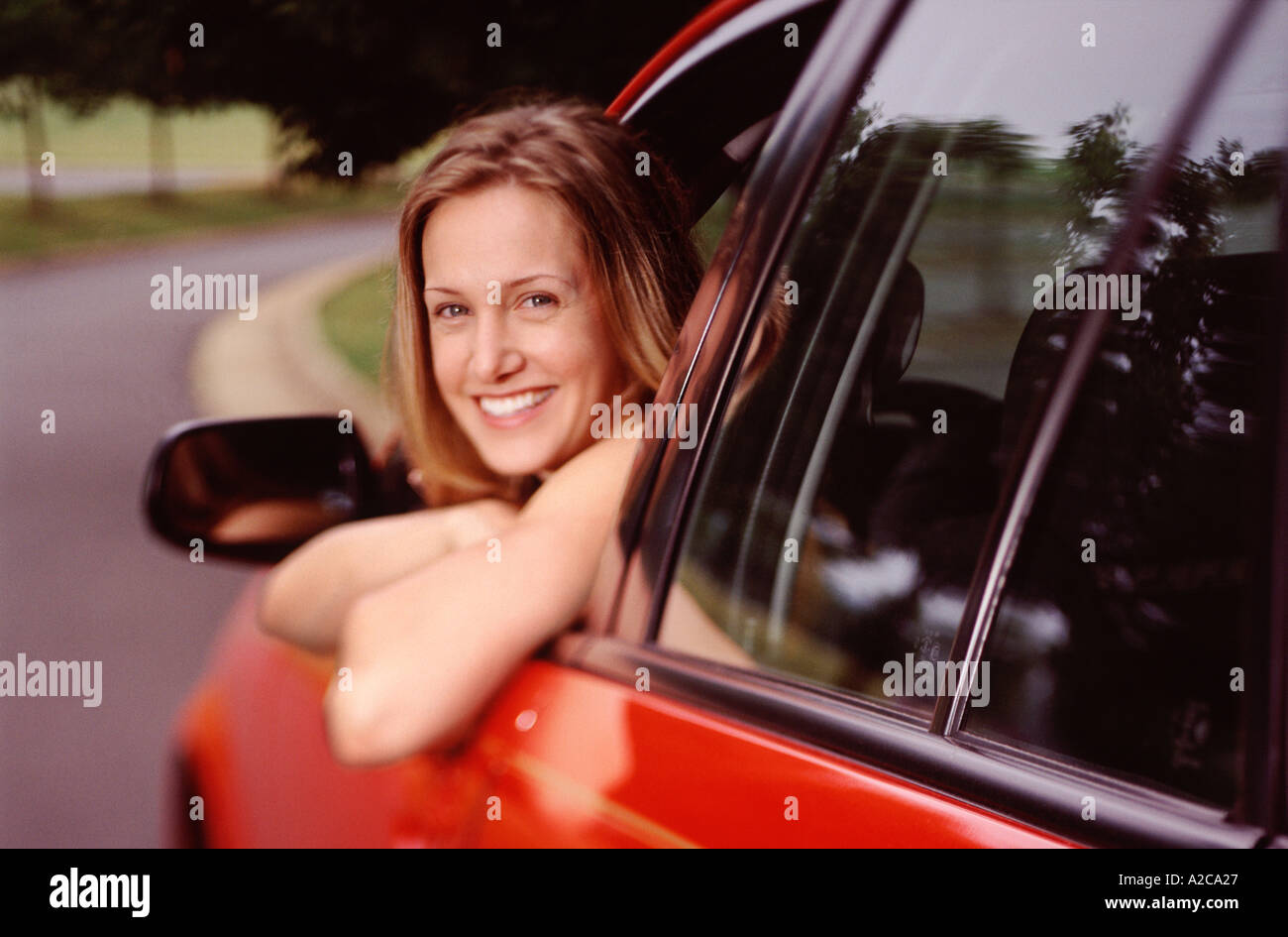 young smiling blonde woman looking out of car driver's side window ...