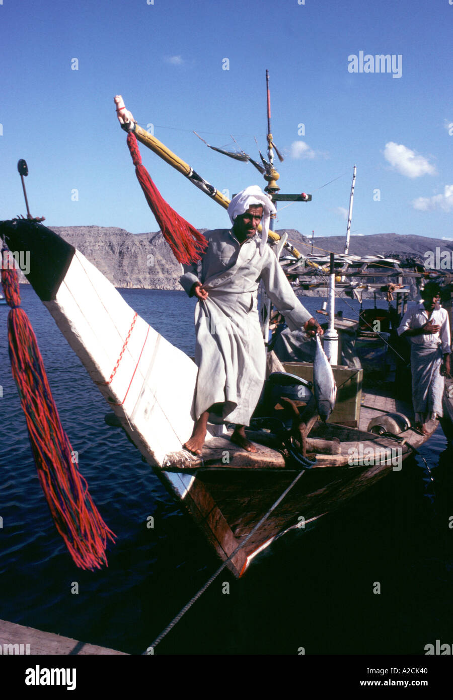 Oman. Musandam. Man getting off a dhow in Khasab carrying a fish they ...