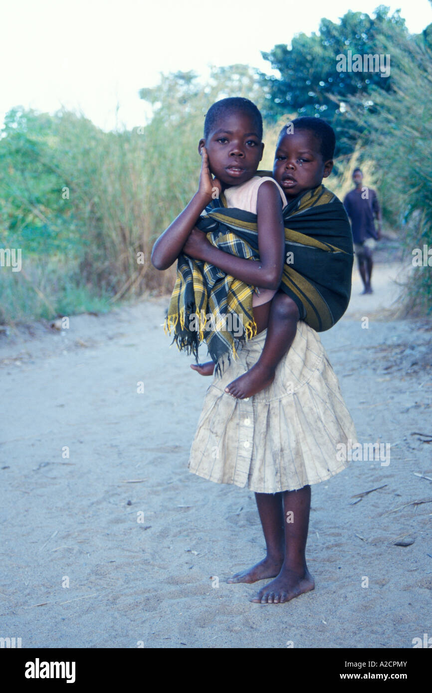a girl carrying her small brother or sister on her back at Kande Beach ...