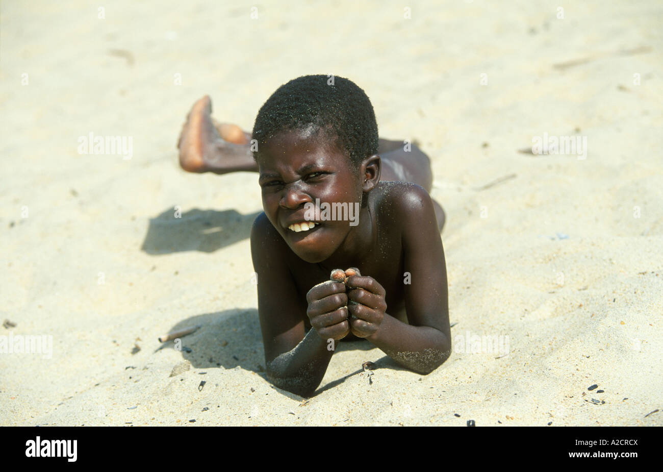 a smiling native boy lying in the sand at Kande Beach at Lake Malawi in ...