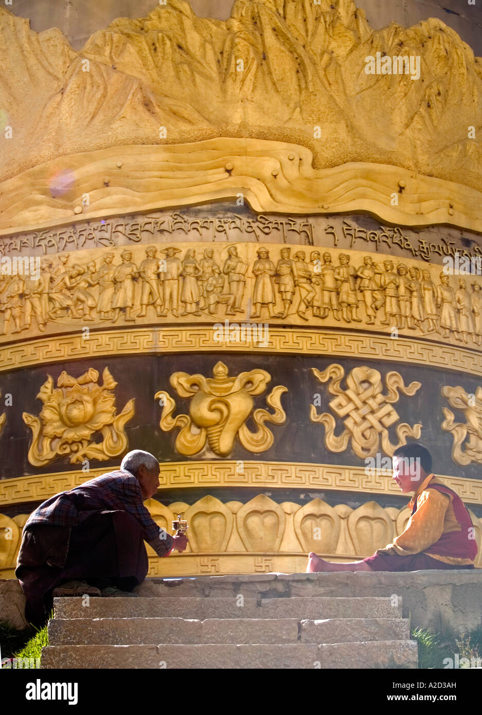 pilgrim and monk beg for alms under giant prayer wheel Shangri La China ...