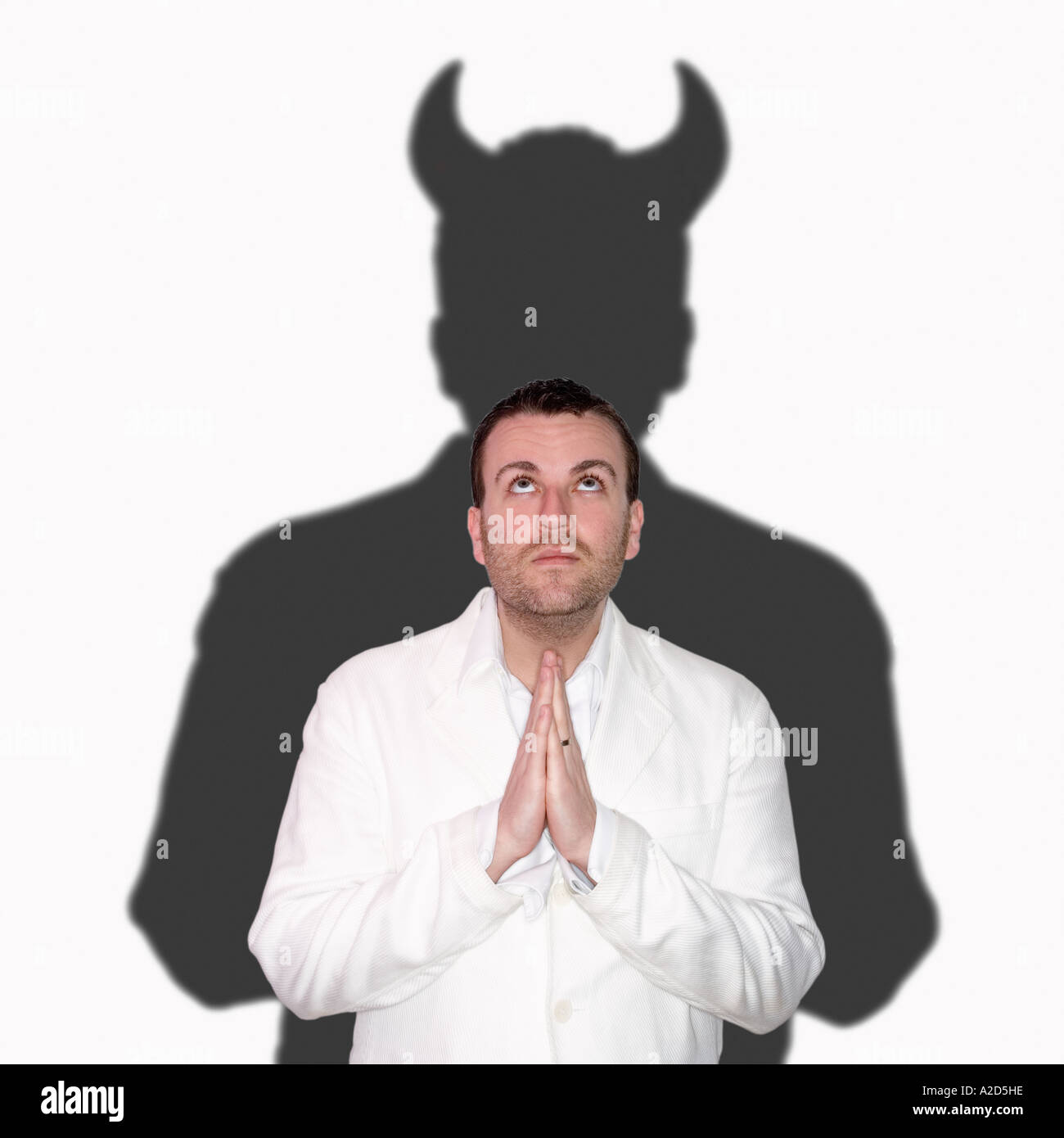 Man in white praying with devil's shadow Stock Photo - Alamy