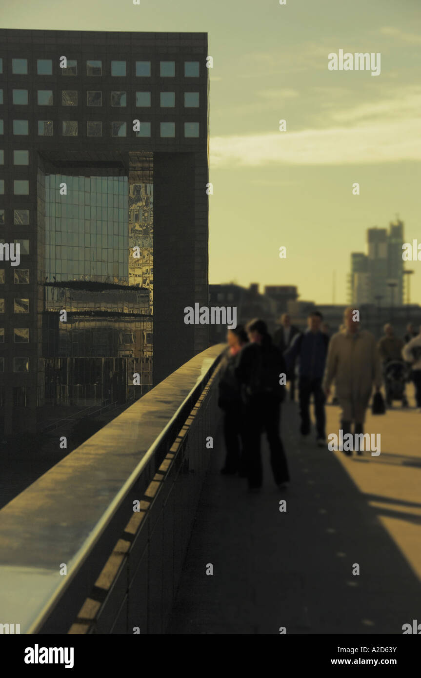 Commuters crossing London Bridge from the south in morning sunlight ...