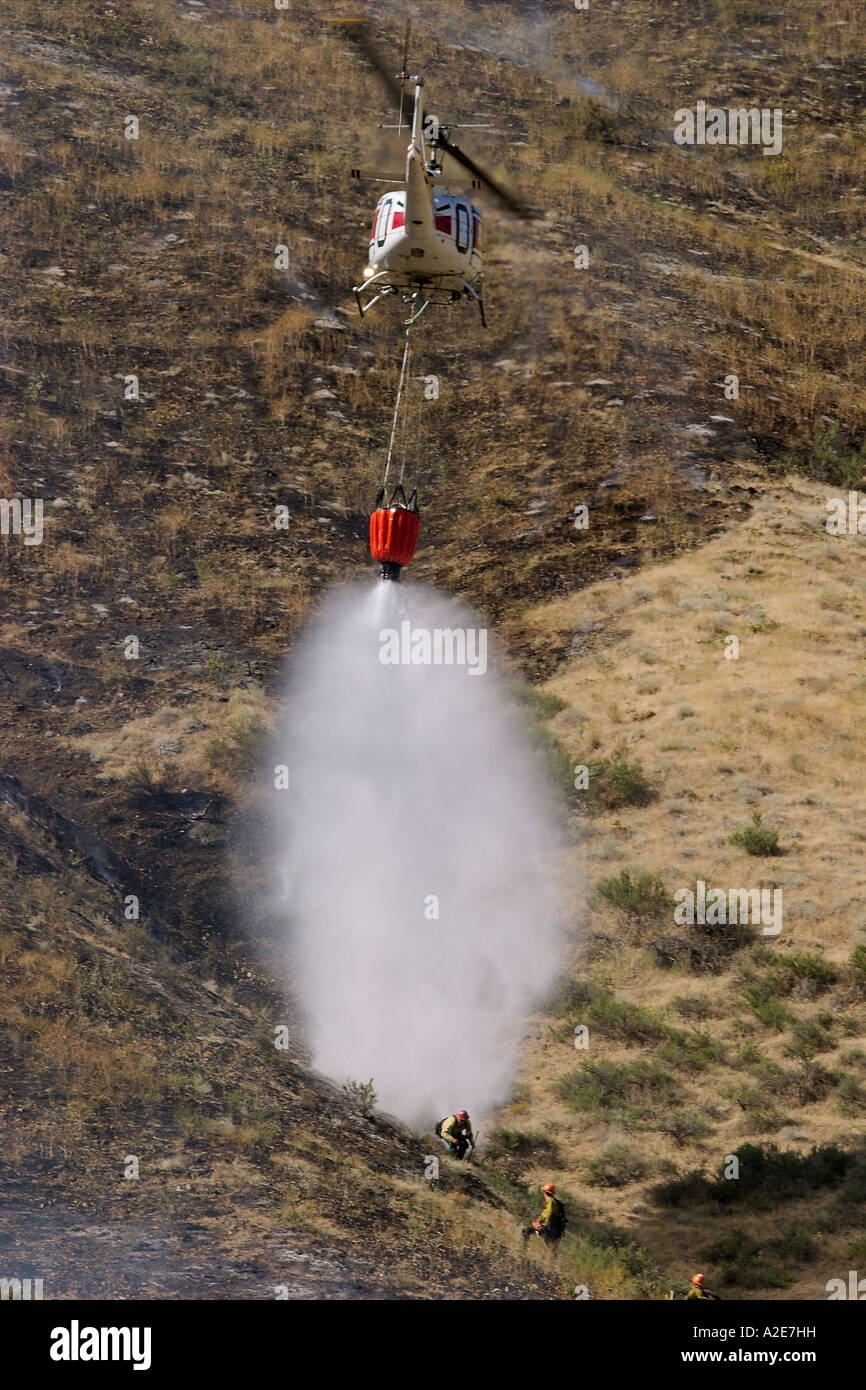Helicopter dropping water at a wildland fire with firemen below Stock ...
