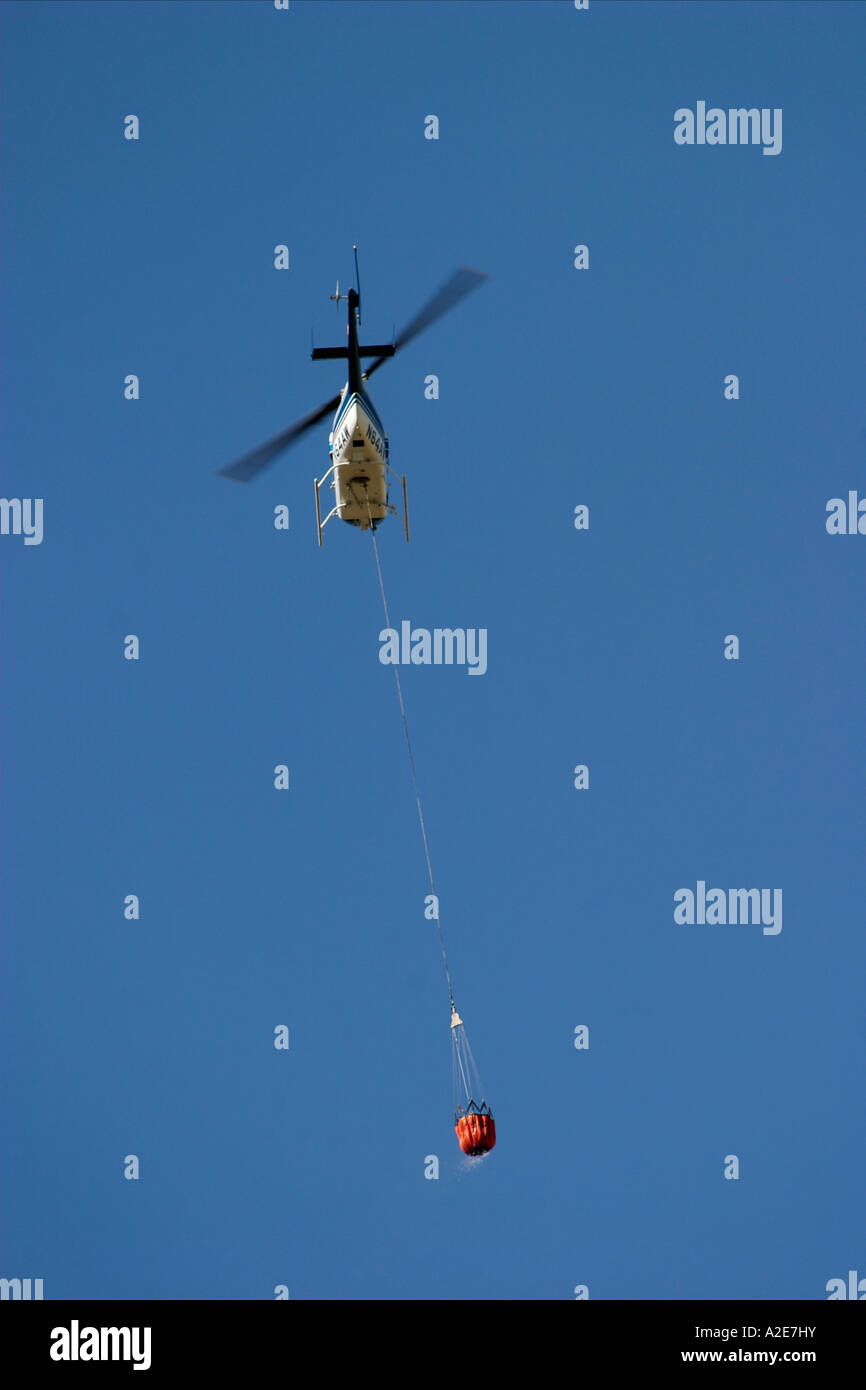 Helicopter carrying water in a bucket to drop on a forest fire with a ...