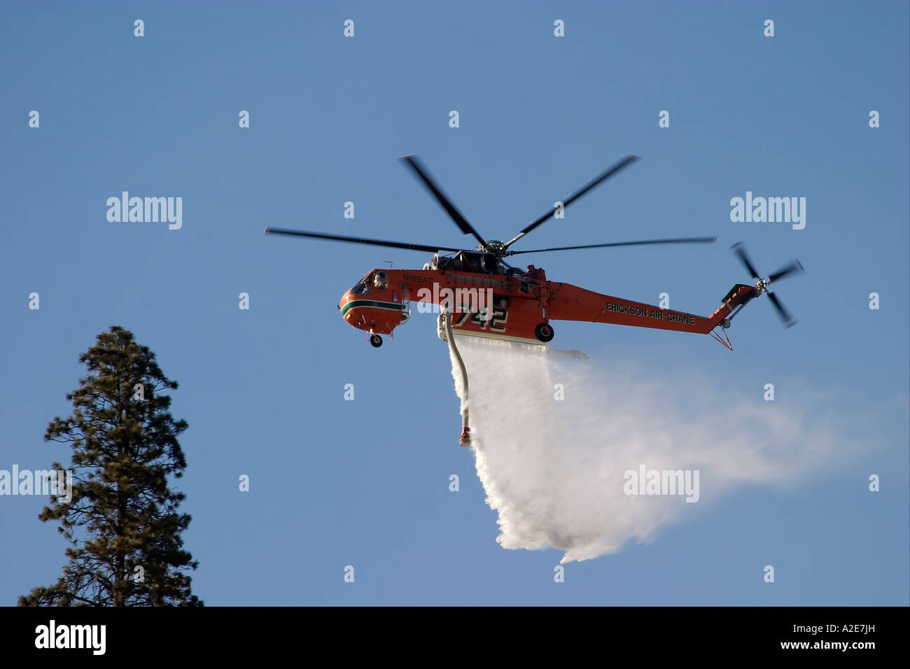 Sikorsky helicopter dropping water on a forest fire against a blue sky ...