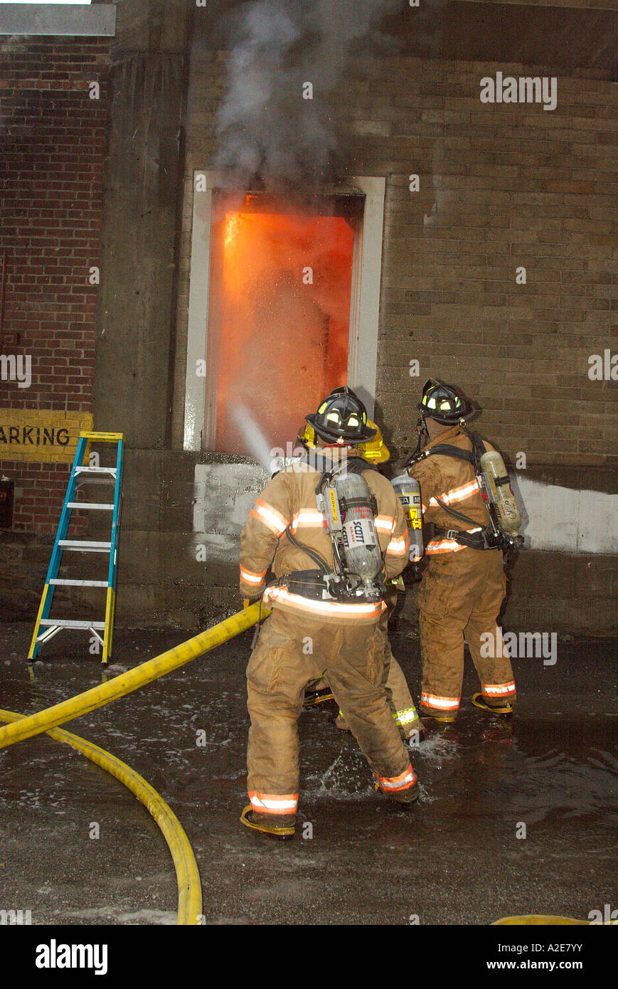 Firemen spraying water into a doorway of a brick commercial warehouse ...