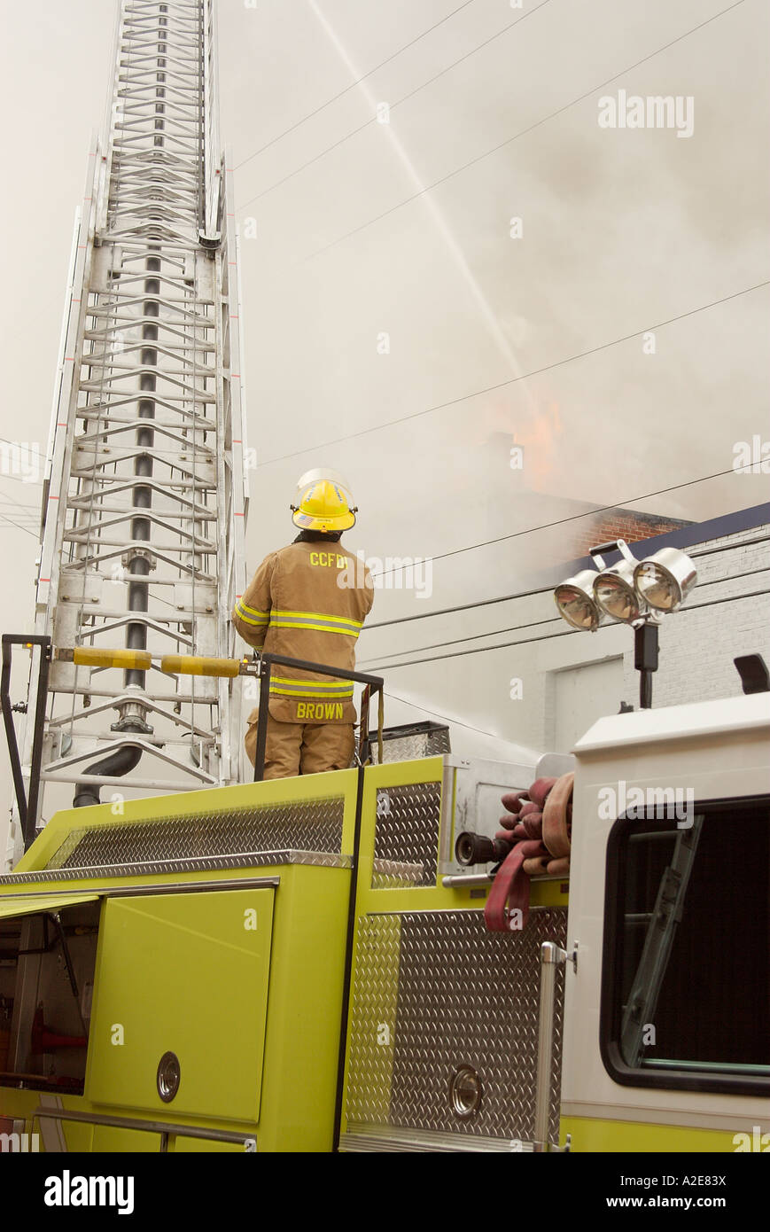Firemen operating the ladder for a fireman spraying water onto a brick ...
