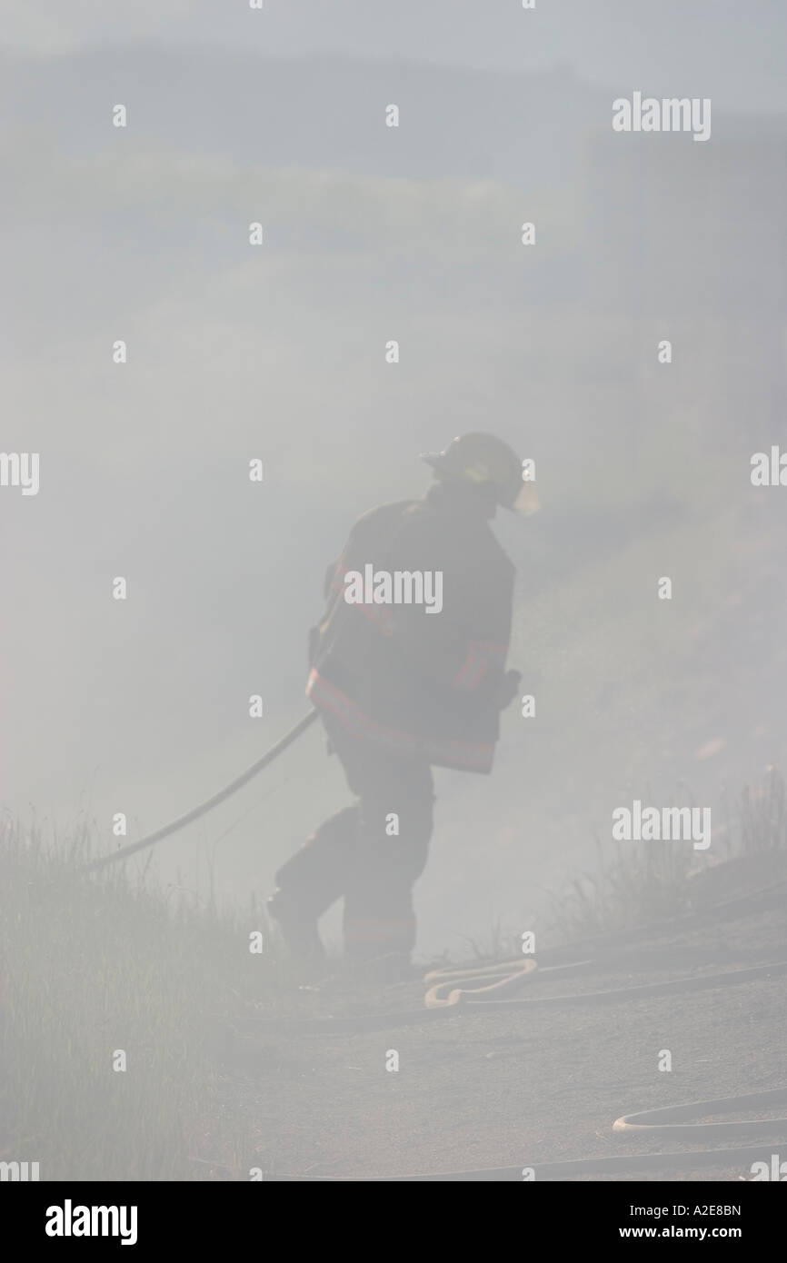 Fireman spraying water on a brush fire barely visable in the smoke ...