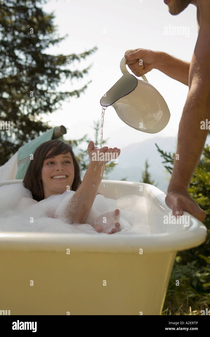 Young woman lying in bathtub, young man pouring water Stock Photo - Alamy
