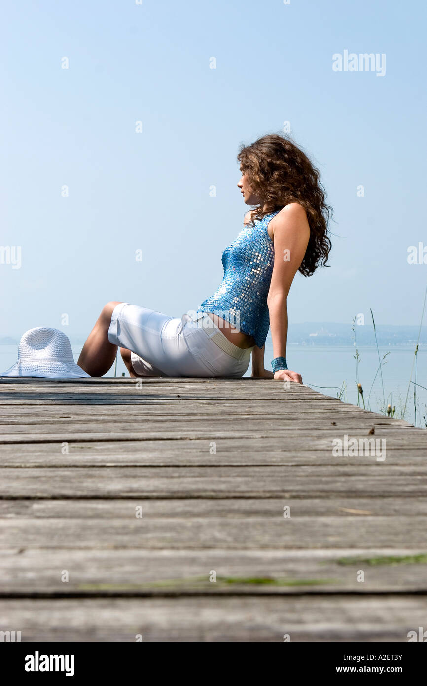 Young woman sitting on jetty, side view Stock Photo - Alamy