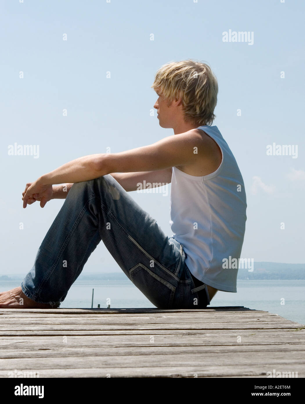 Young man sitting on jetty, side view Stock Photo - Alamy