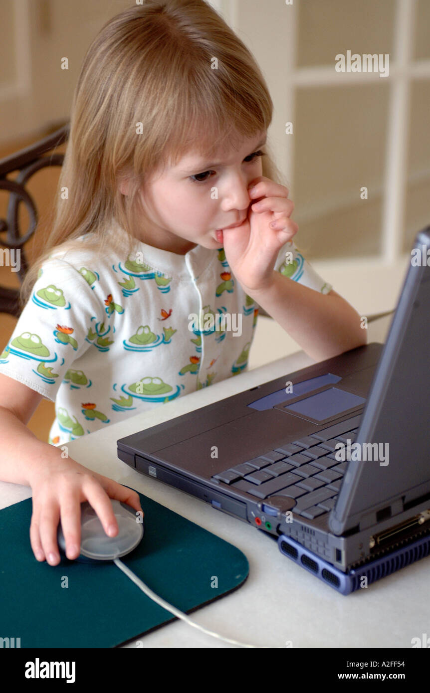 A young girl sucks her thumb problem solving on her laptop computer ...