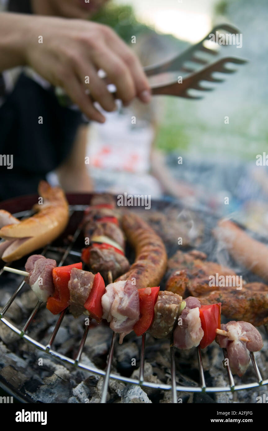Meat and sausages on grill people in background Stock Photo - Alamy