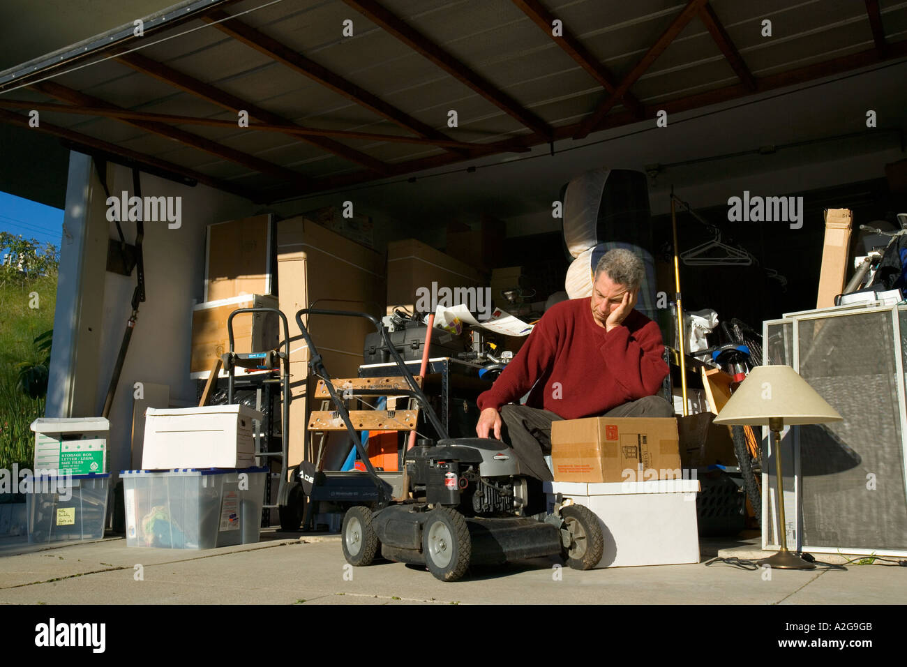 Middle aged white man sits amongst all the junk in his garage looking ...