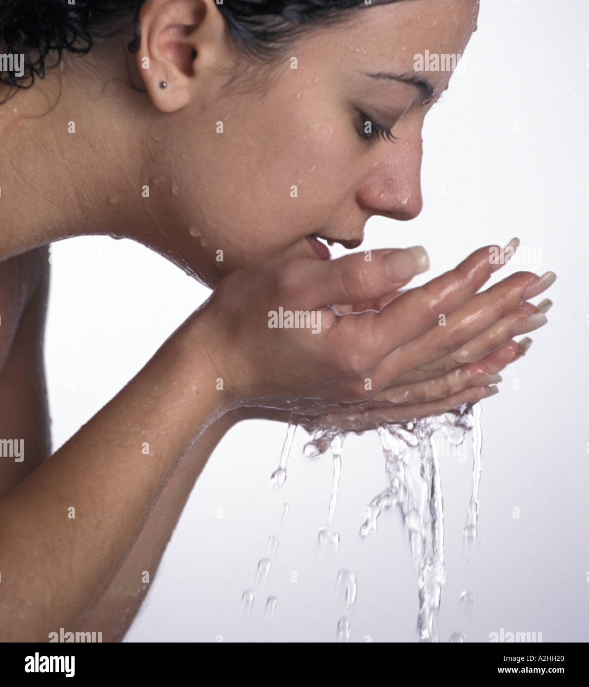 Close up of a Caucasian woman washing her face with water on a white ...