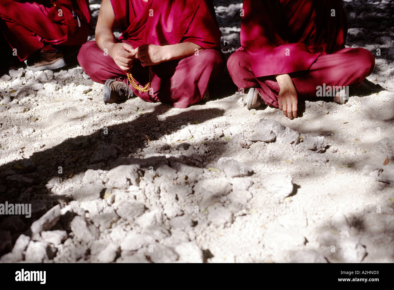 Two sitting Buddhist monks wearing red robes holding wooden prayer ...