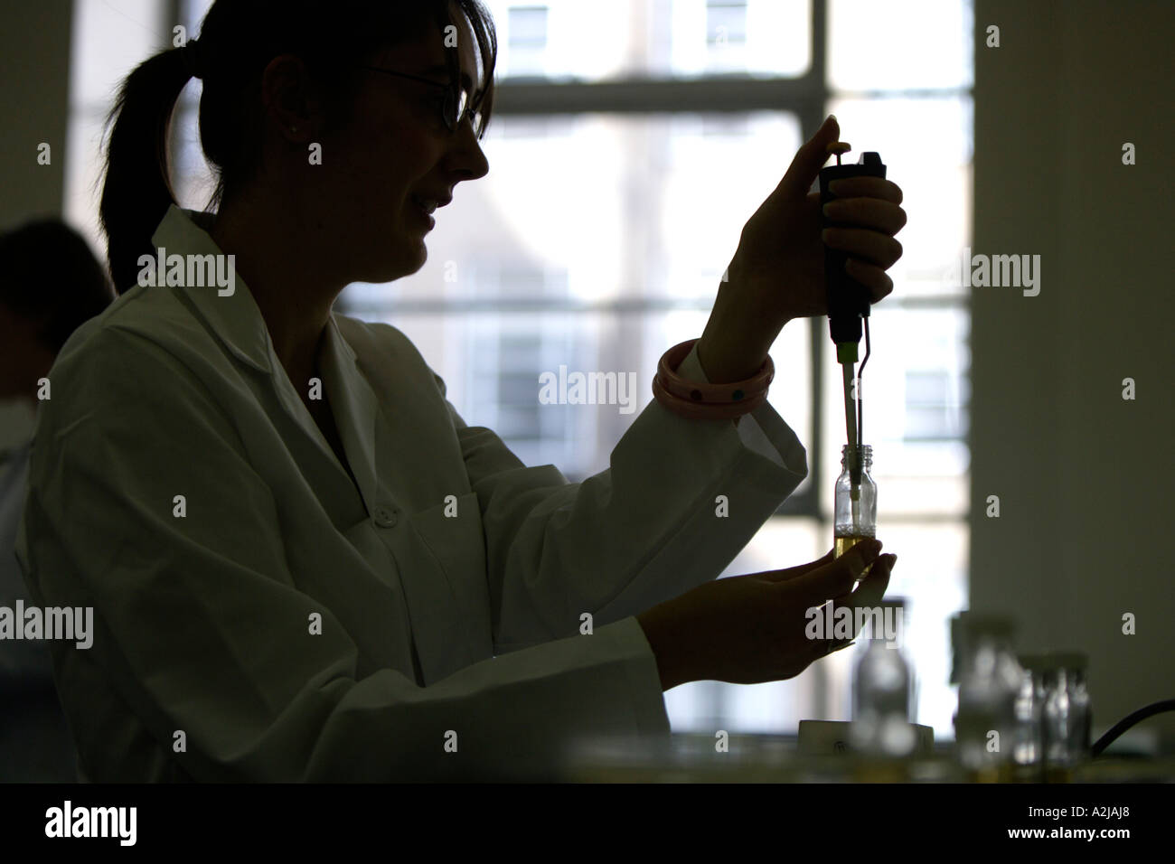 A lab scientist drops liquid into a bottle using a pipette during a ...