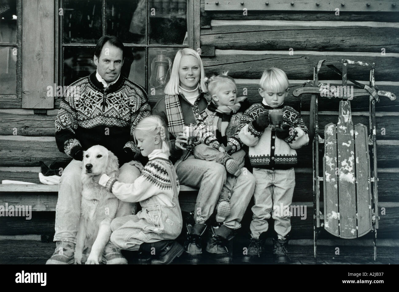 A couple and three children together outside a log cabin on a chilly ...