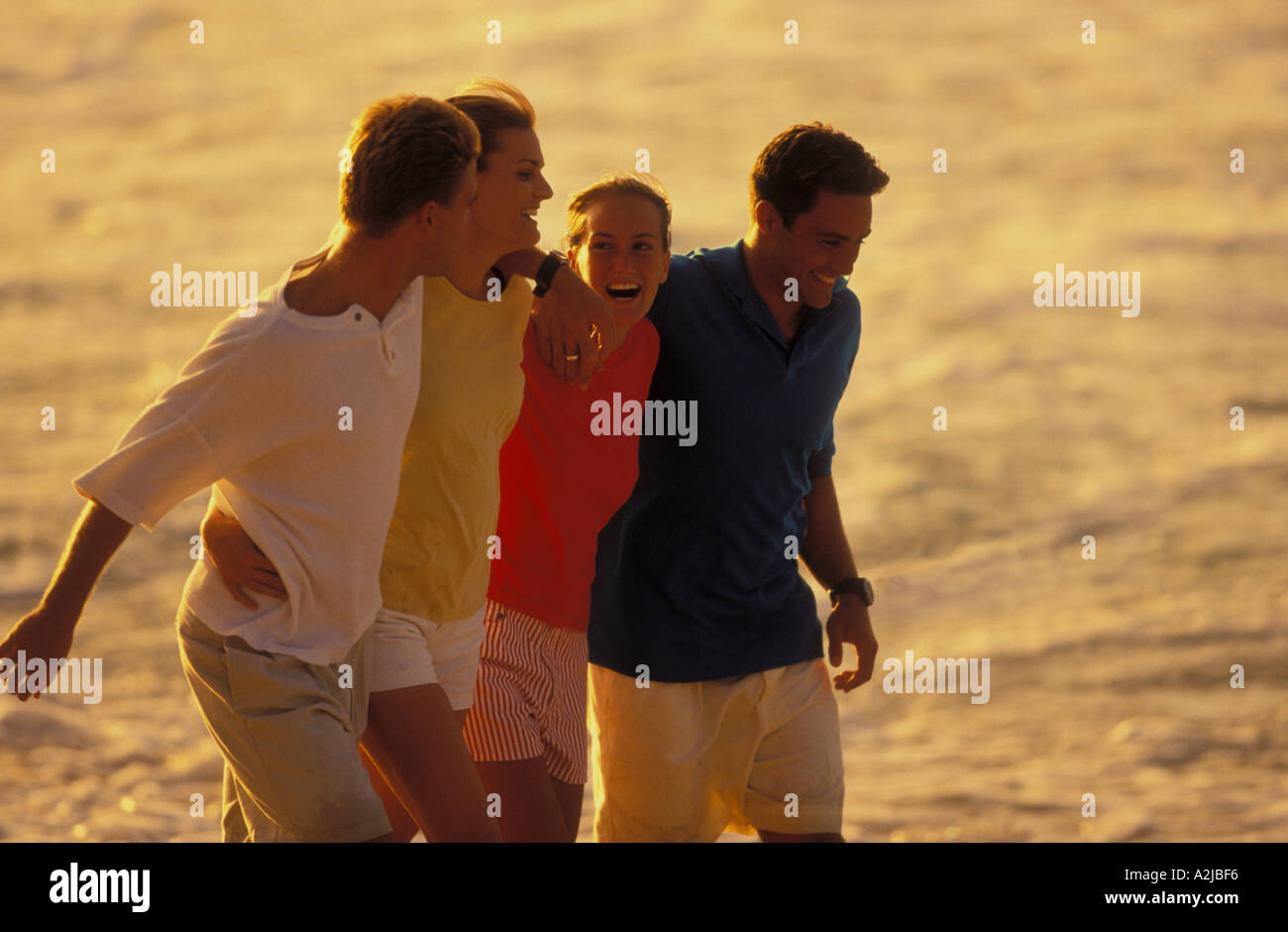 Two happy couples walk along a beach with their arms around each other ...