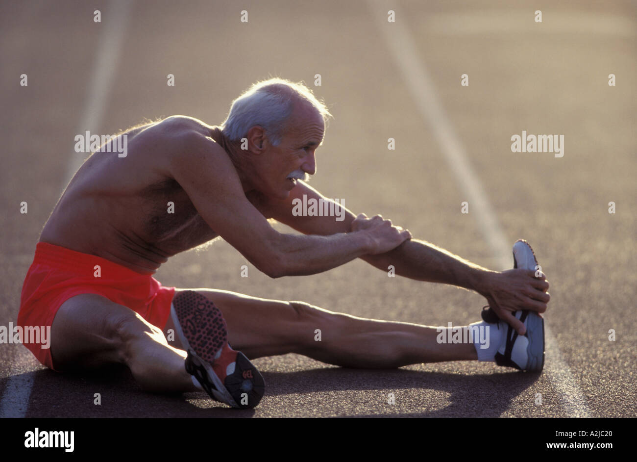 Senior shirtless man doing stretching sit ups on an outdoor track Stock ...