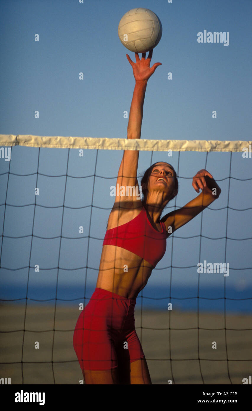 Woman leaping upwards and stretching to spike a volleyball over the net ...