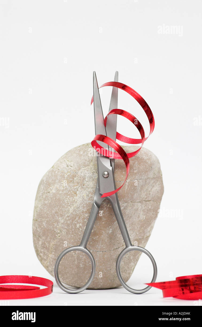 Scissor with cut red tape against rock Stock Photo - Alamy