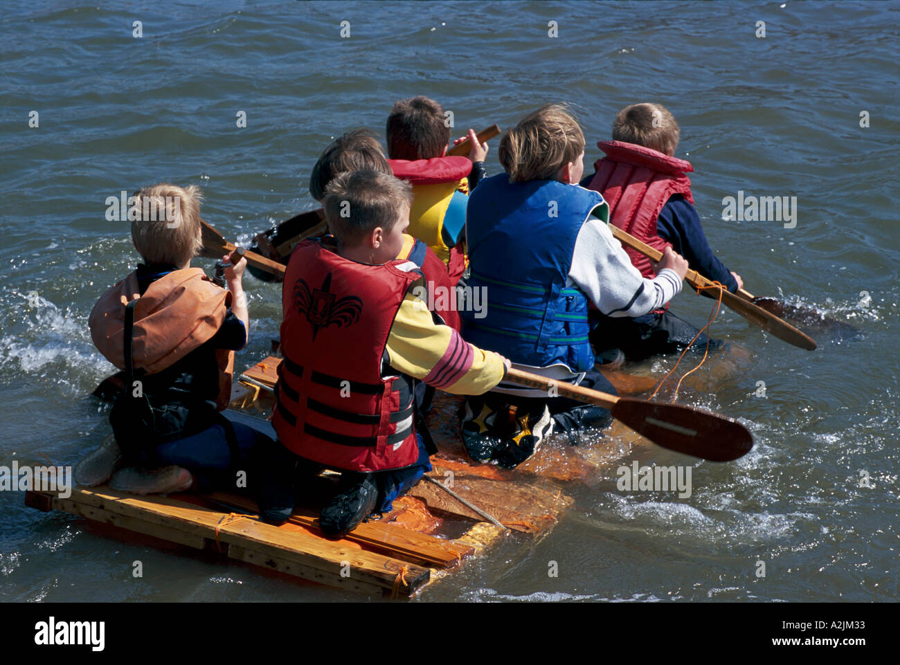 Cub Scout children with backs to viewer having fun rowing on a raft UK ...