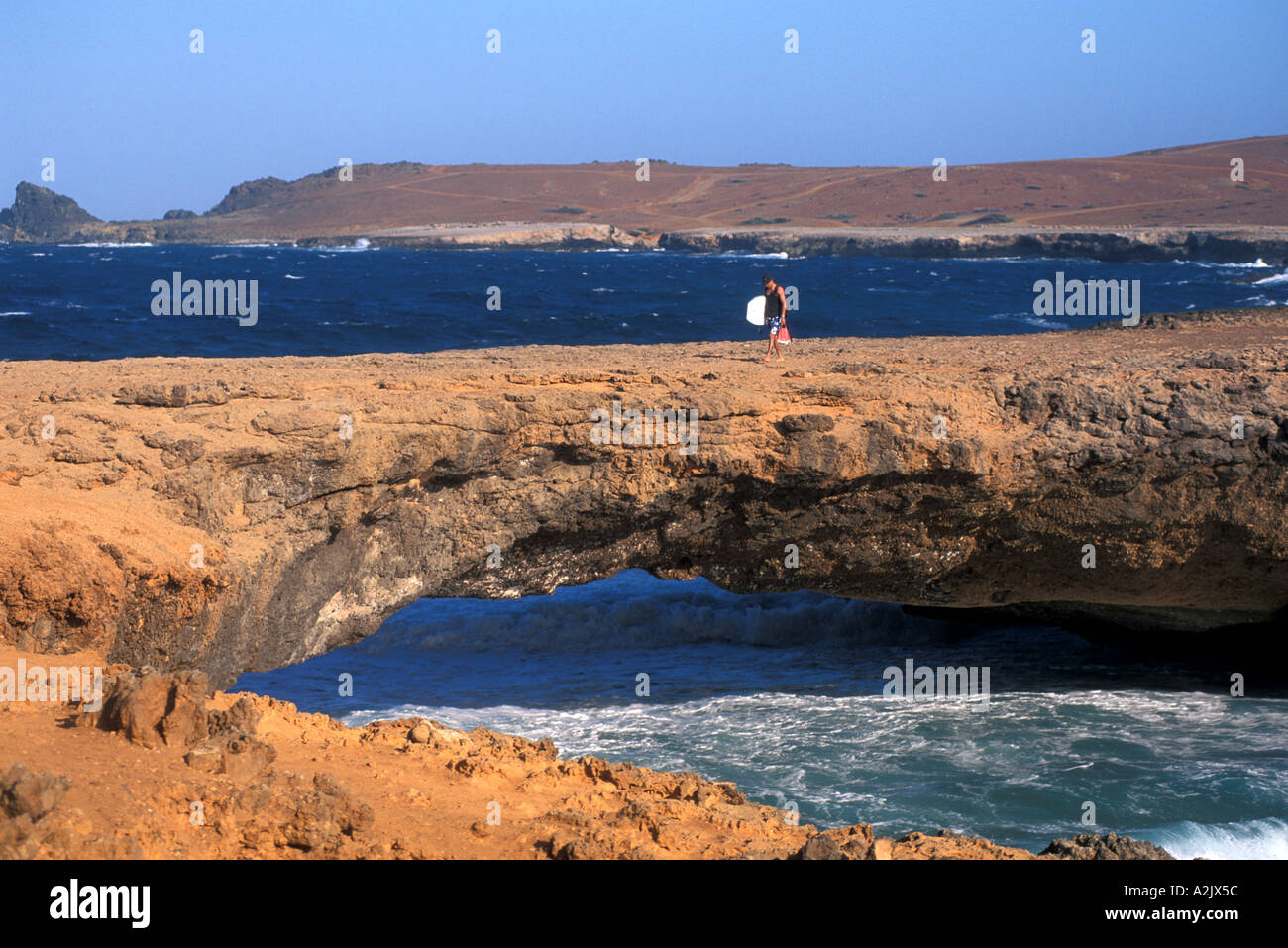 Aruba Natural Bridge with surfer walking across Stock Photo - Alamy