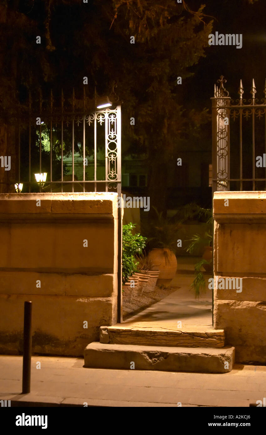 An open gate in a stone wall lit by strong overhead floodlight at night ...