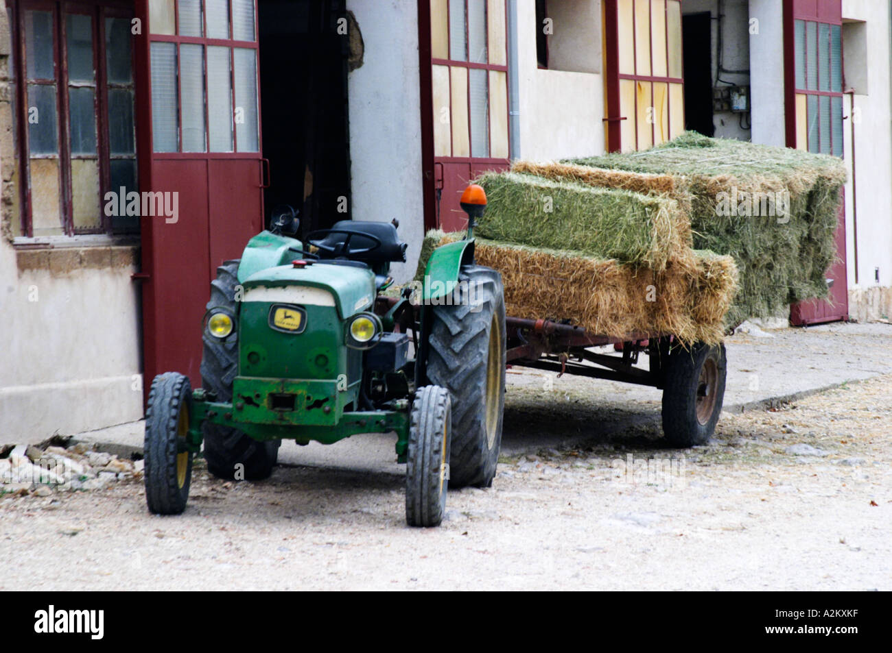 An old rusty green tractor John Deere drawing a cart filled with hay ...
