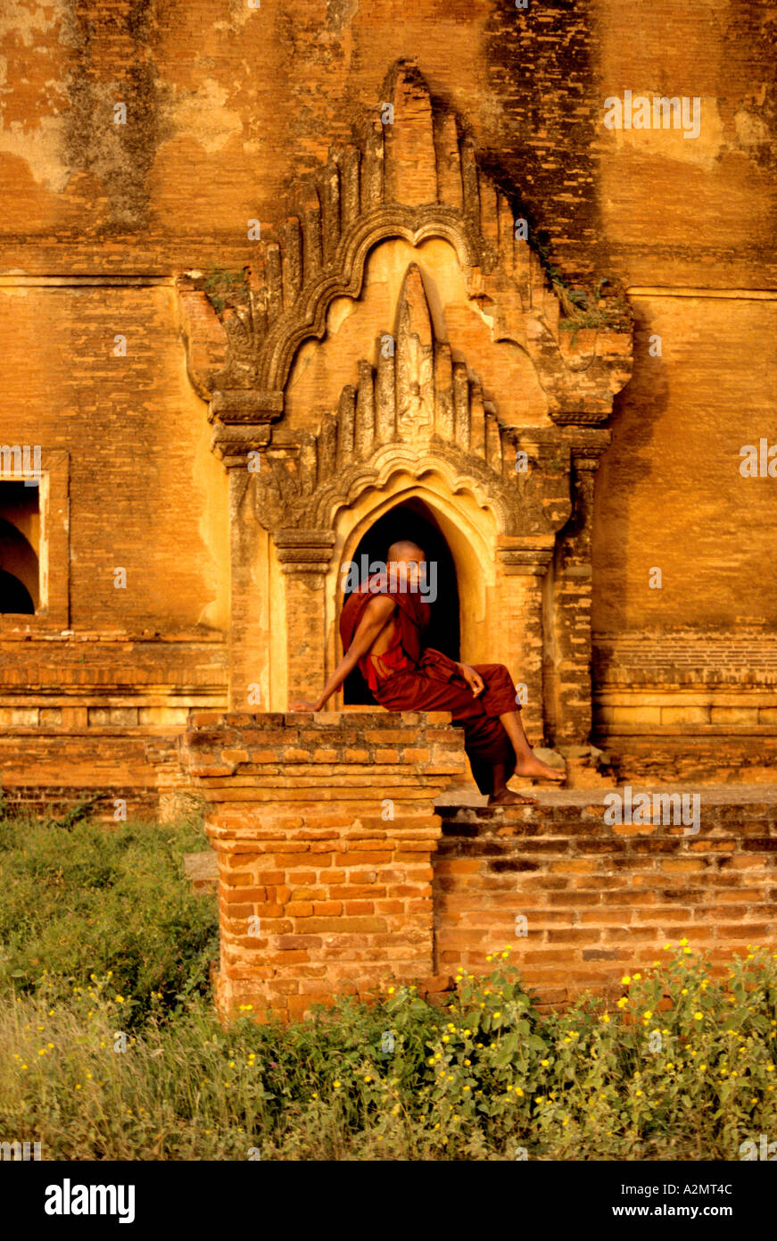Burmese monk in traditional red robes sits outside the mellow Mingun ...