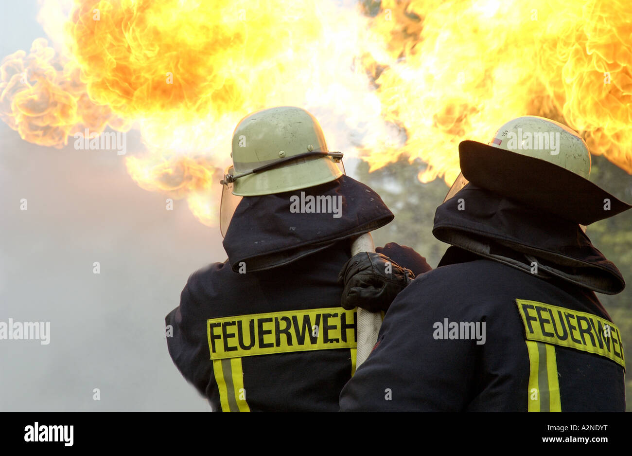 Rear view of two firefighters extinguishing fire Stock Photo - Alamy