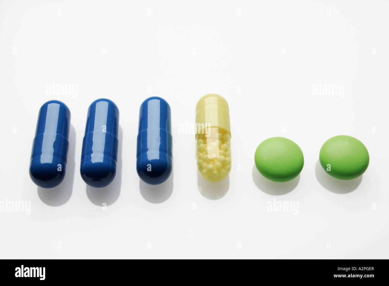 Pills and capsules of different colours in a row, white background ...
