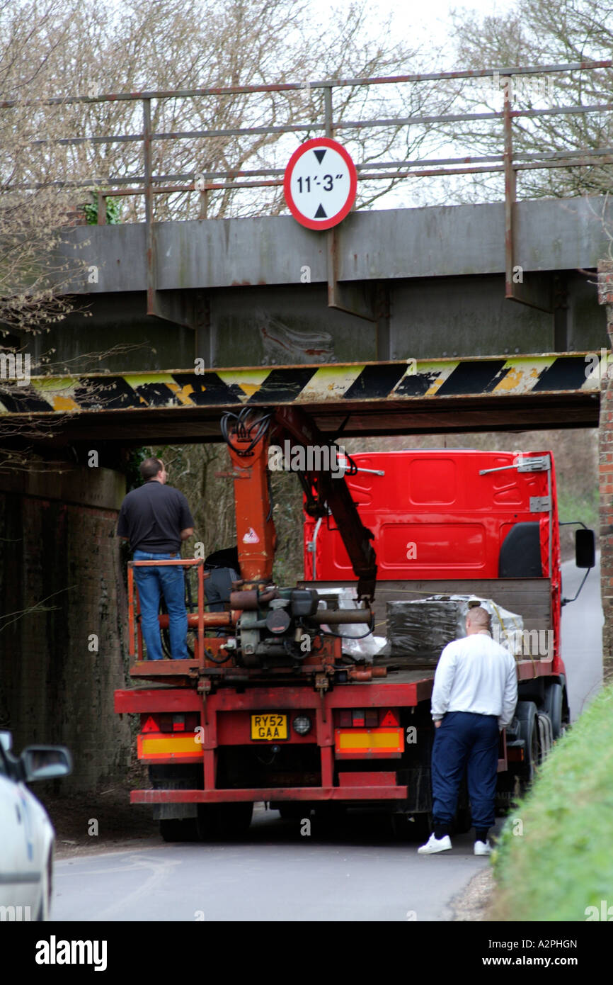 An articulated lorry stuck under a low bridge on an English country ...