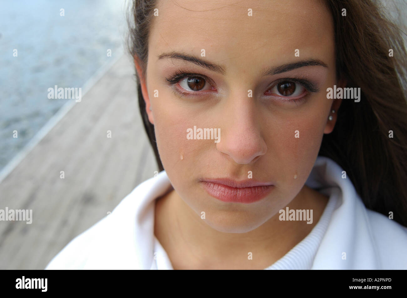 Sad young brunette woman crying on pier with blue water Stock Photo - Alamy