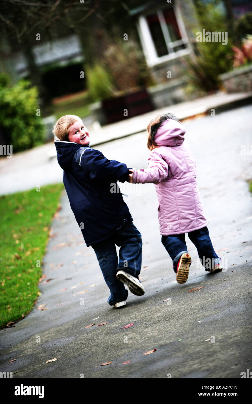 A young boy and girl running down a park path looking back towards the ...